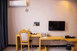 Quarto de hotel com escrivaninha de madeira, uma cadeira, televisão de tela plana e ar condicionado fixado na parede.