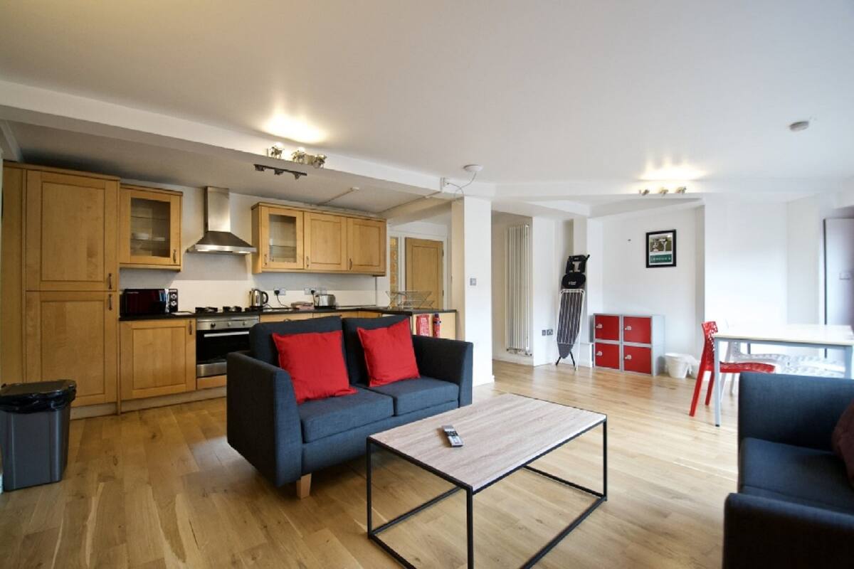 Uma sala de estar moderna com sofá, mesa de centro e área de cozinha com armários e eletrodomésticos de madeira.