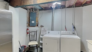 Uma lavanderia com máquina de lavar, secadora e uma cadeira.