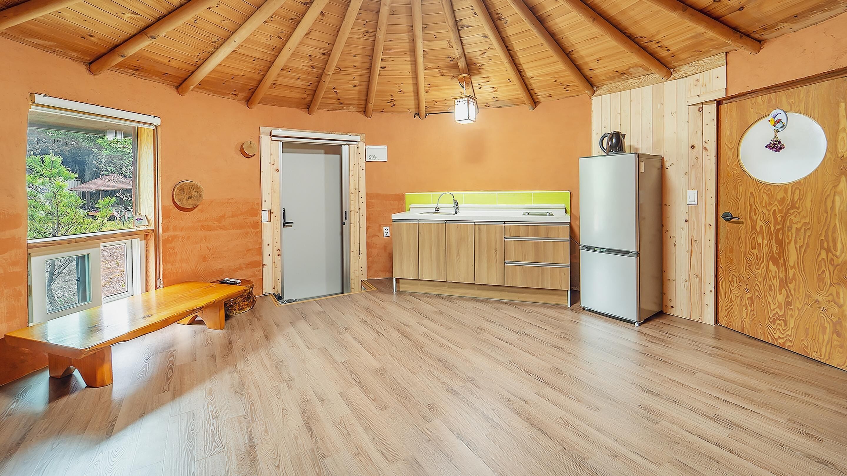 Cozinha compacta com armários de madeira, pia e geladeira. Há um banco e uma porta que dá para outro cômodo.