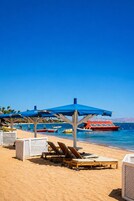 Uma praia com espreguiçadeiras, guarda-sóis e um barco vermelho na água.