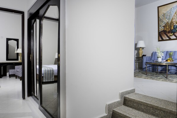 Quarto de hotel com uma cama, uma escrivaninha com luminária, uma cadeira e uma janela.