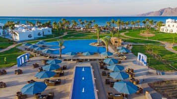 Um resort com piscina central, áreas de estar e vista para o mar.