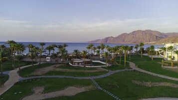Um resort com área de piscina, palmeiras e vista para o mar e montanhas.