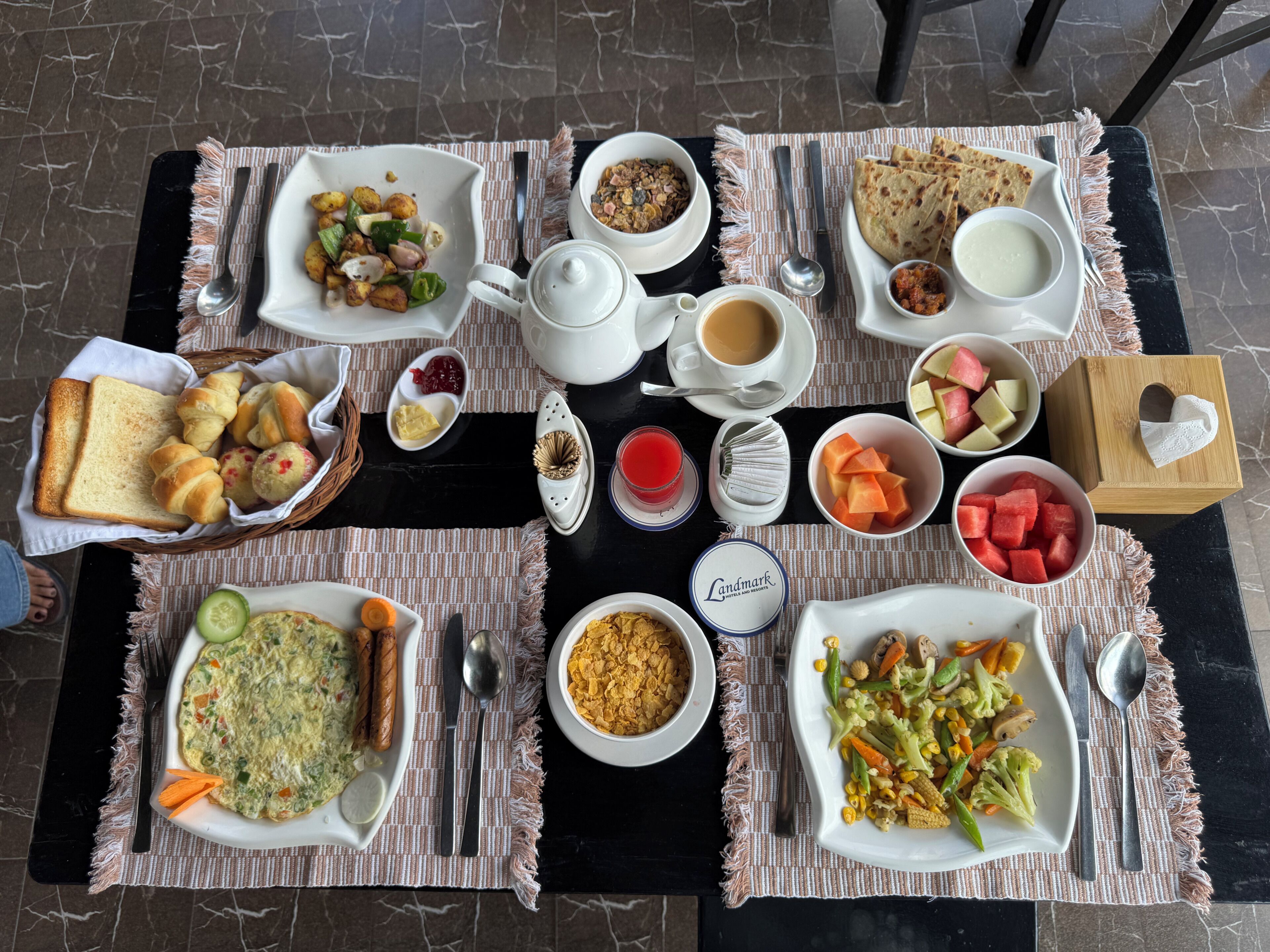 Um buffet de café da manhã com diversos pratos, utensílios e uma caixa de guardanapos.