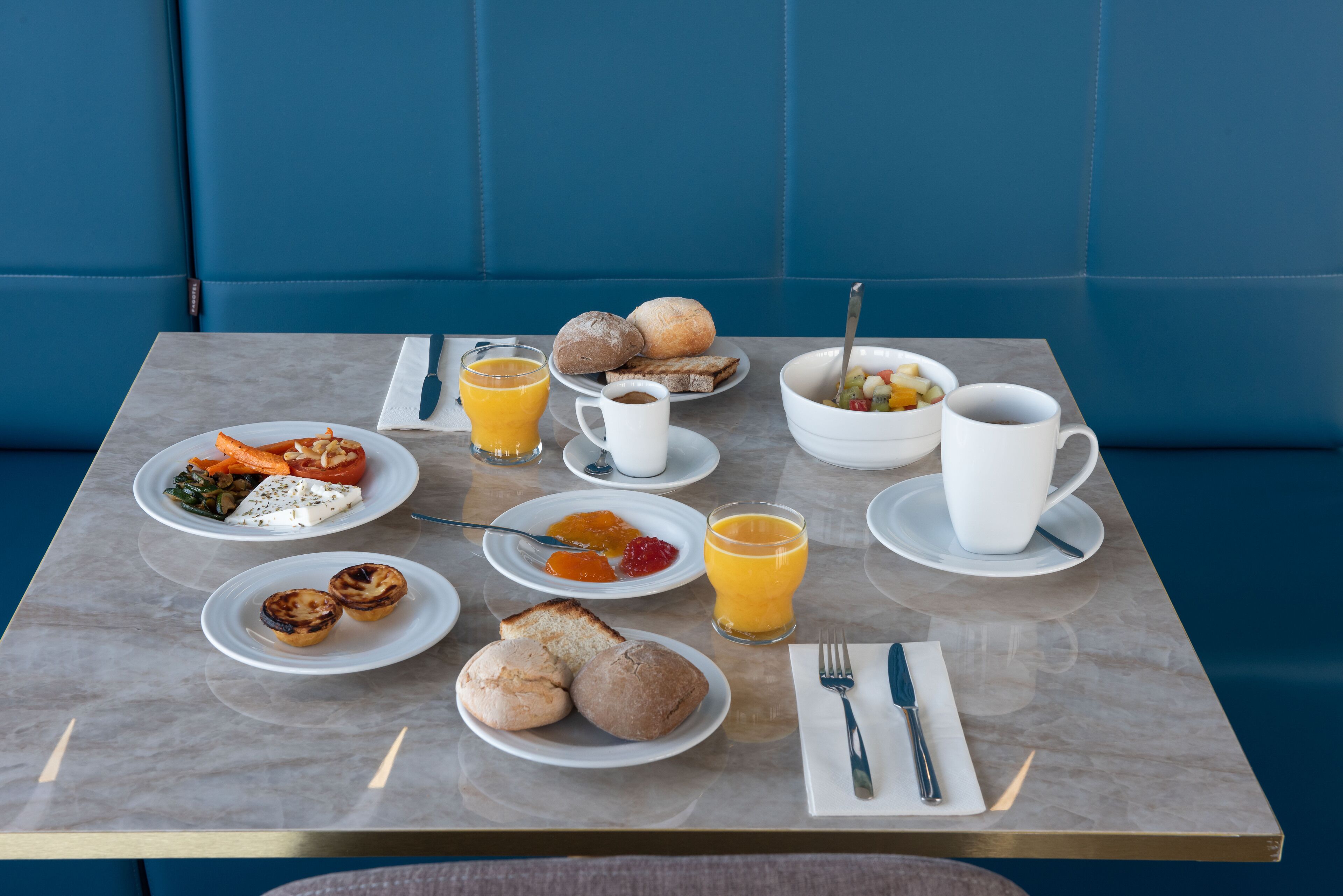 Uma mesa de café da manhã com pratos de comida, uma tigela de frutas e dois copos de suco de laranja.