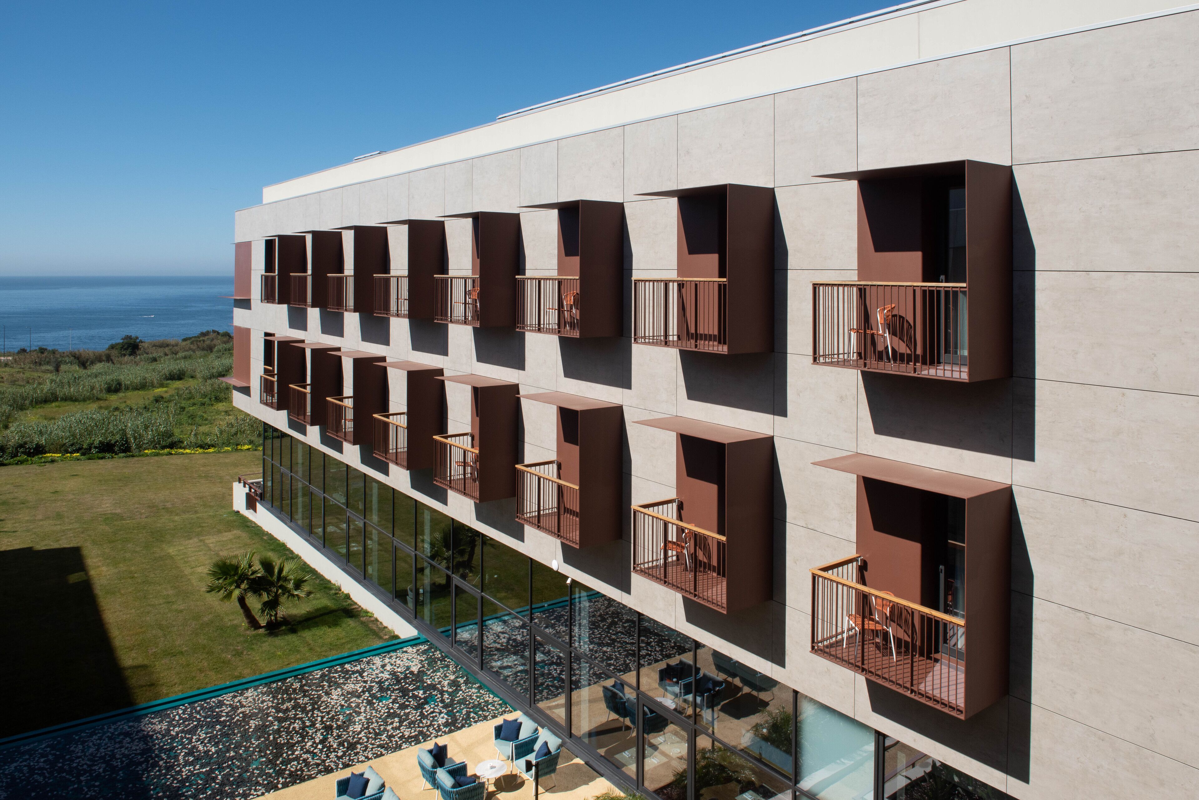 Um hotel moderno com várias varandas, área de piscina e vista para o oceano.