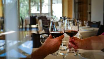 Duas mãos segurando copos de vinho numa mesa em restaurante, com vista para o exterior.