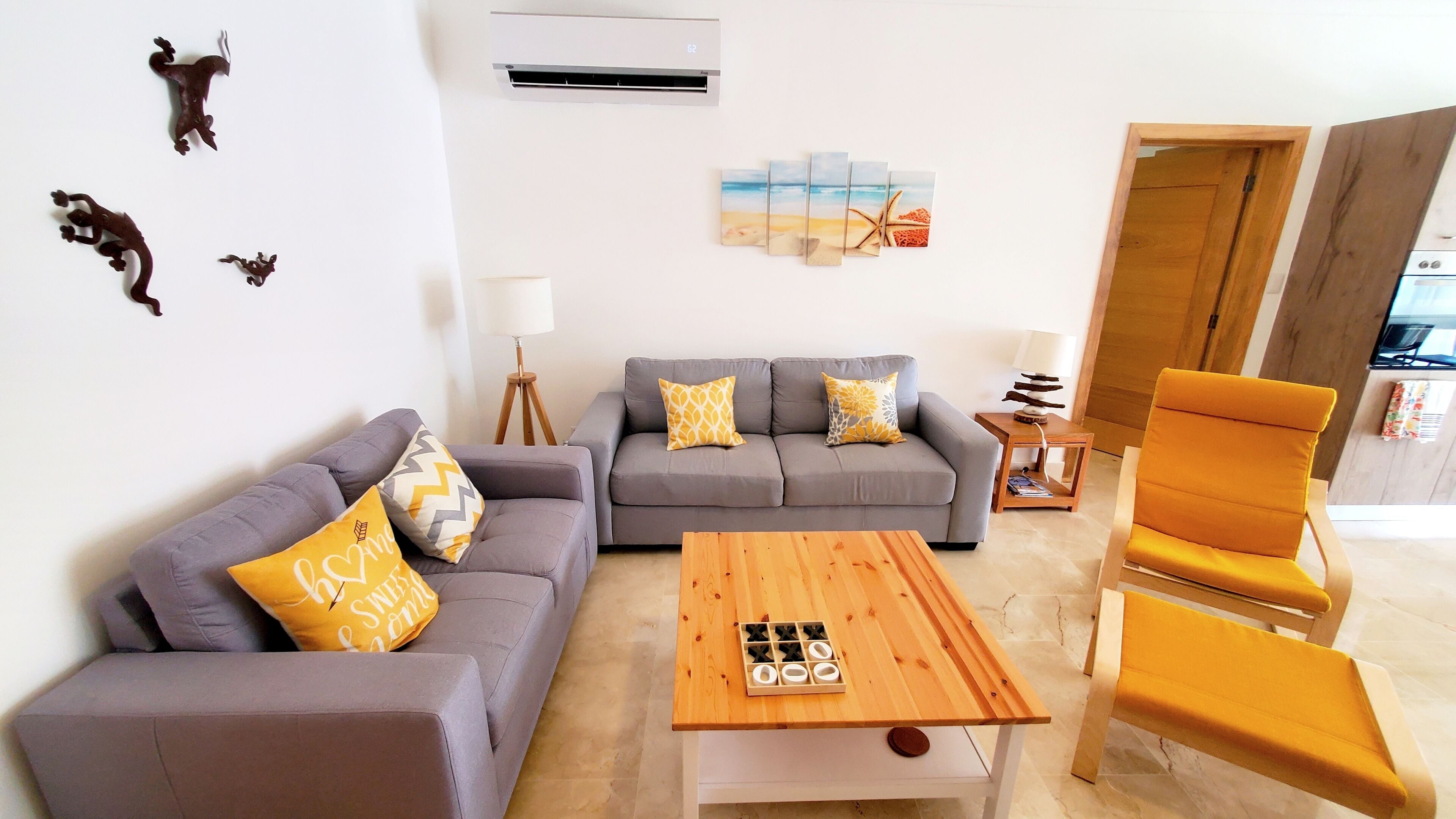 Uma sala de estar com um sofá cinzento, uma mesa de centro de madeira e uma poltrona amarela.