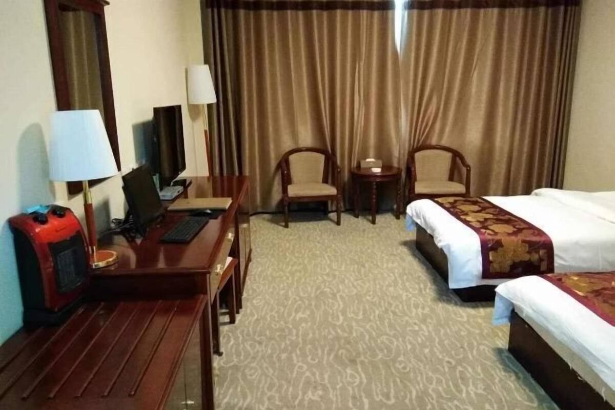 Quarto de hotel com escrivaninha, duas cadeiras, uma cama e uma mesinha.
