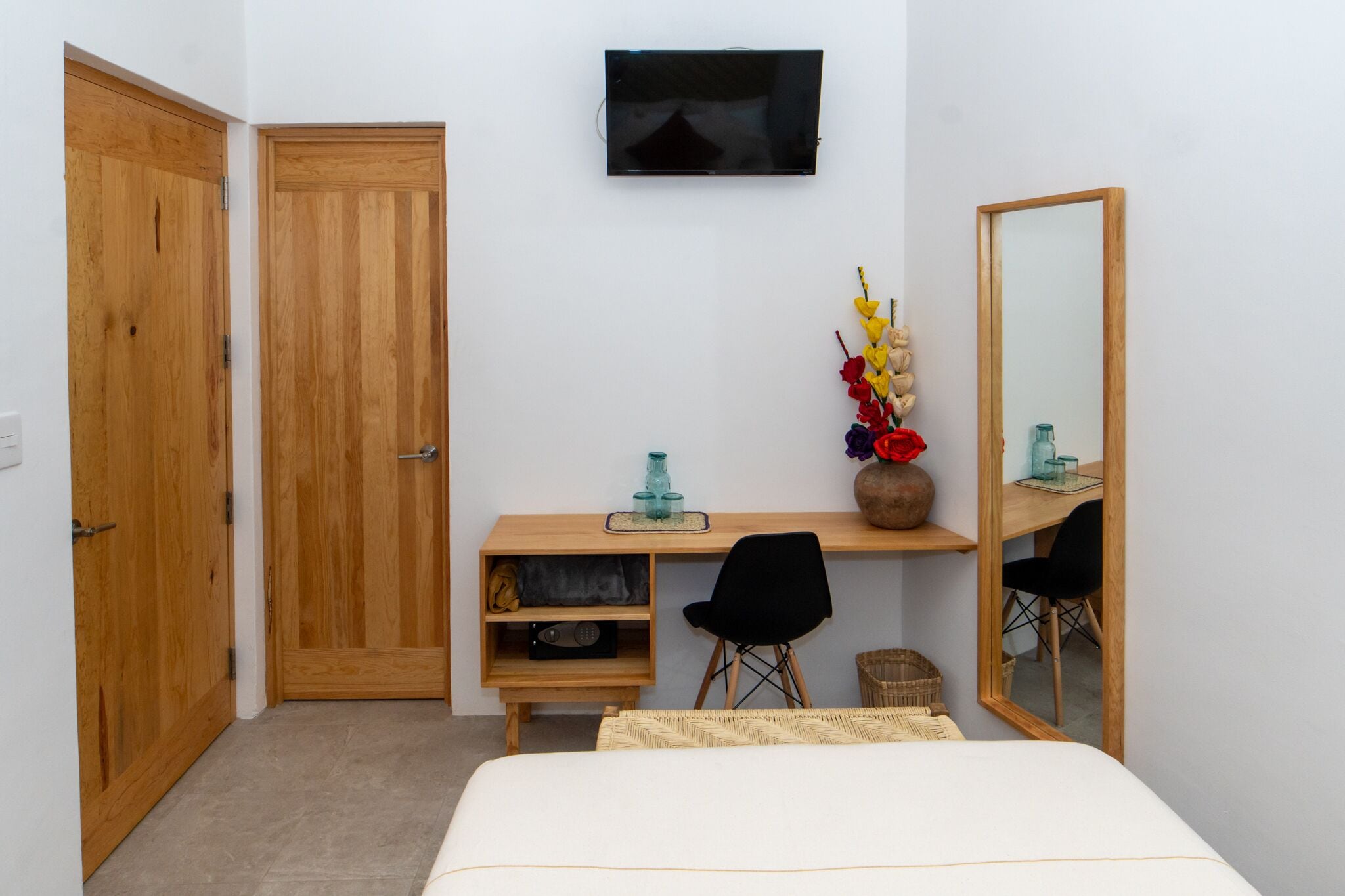 Quarto com cama, escrivaninha, cadeira, espelho e duas portas de madeira.