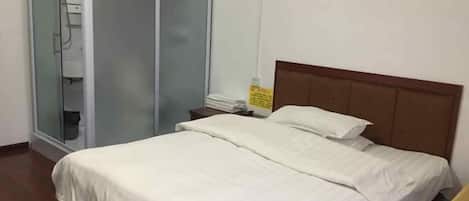 Quarto com cama, mesa de cabeceira, telefone fixado na parede e porta com painéis de vidro jateado.