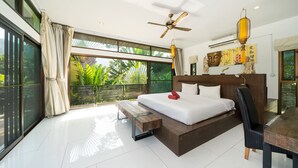 Quarto moderno com uma cama grande, um ventilador de teto e vista para um verde exuberante.