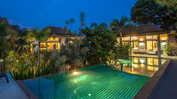 Piscina com borda revestida, cercada por vegetação exuberante e palmeiras.