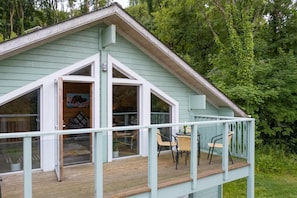 Uma cabana verde-clara com um deck de madeira e uma área de estar coberta ao ar livre.