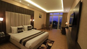 Quarto de hotel com uma cama grande, televisão de tela plana, escrivaninha e varanda com vista para a cidade.
