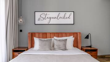 Uma cama bem arrumada com cabeceira, duas mesas de cabeceira, um aplique de parede e uma placa emoldurada com o texto #Stayunlocked.