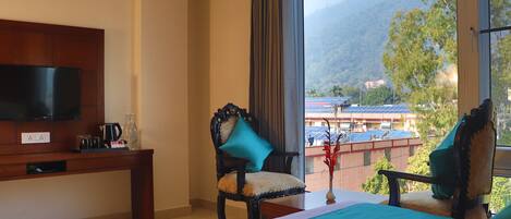 Quarto de hotel com cama, escrivaninha e televisão, e duas cadeiras.