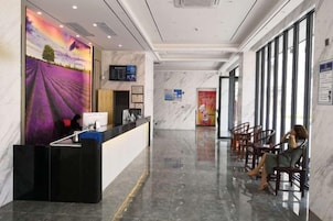Uma área de recepção de hotel com balcão, espaço para sentar e uma janela grande.