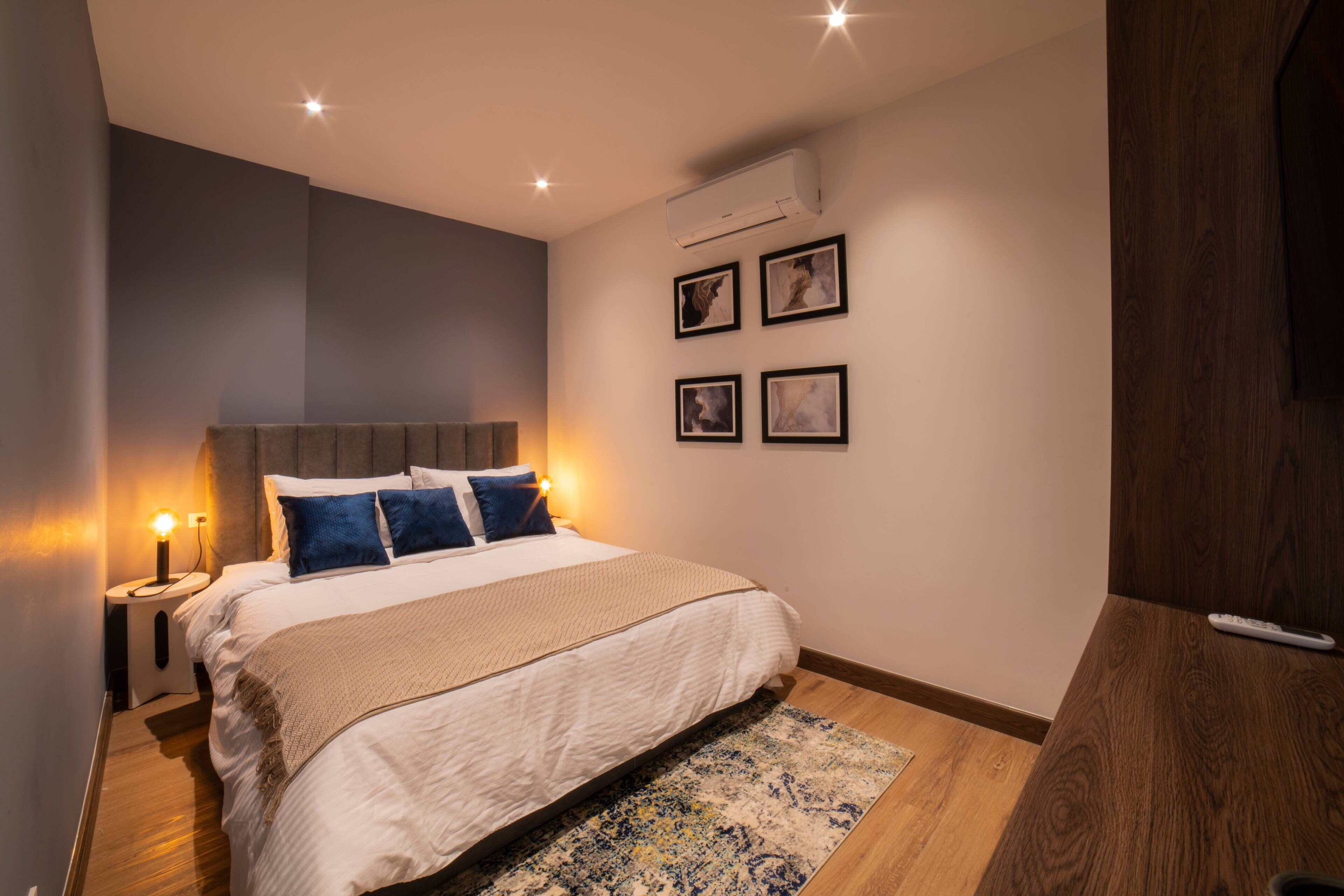 Um quarto moderno com uma cama grande, luminárias de cabeceira, ar condicionado fixado na parede e obras de arte emolduradas.