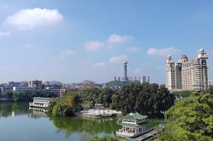 Vista para um lago com um pavilhão tradicional, um barco e edifícios modernos ao fundo.