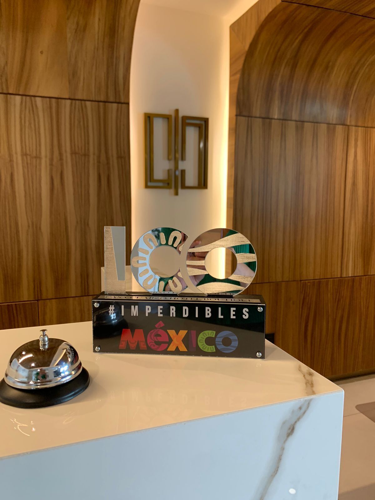 Uma mesa de recepção com uma placa que diz "100 IMPERDIBLES Mexico" e um relógio decorativo.
