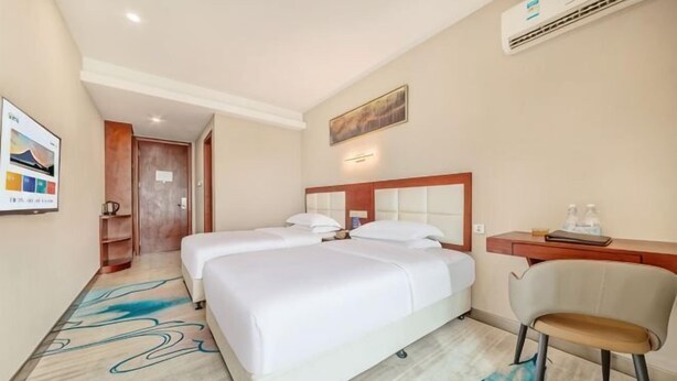Quarto de hotel com duas camas, uma escrivaninha, uma cadeira, um quadro e um aparelho de ar condicionado.