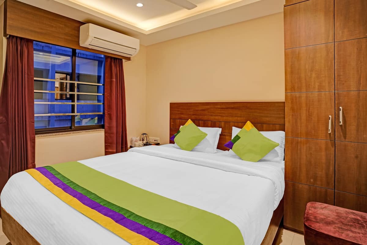 Quarto de hotel com uma cama grande, cabeceira de madeira e uma janela com cortinas.