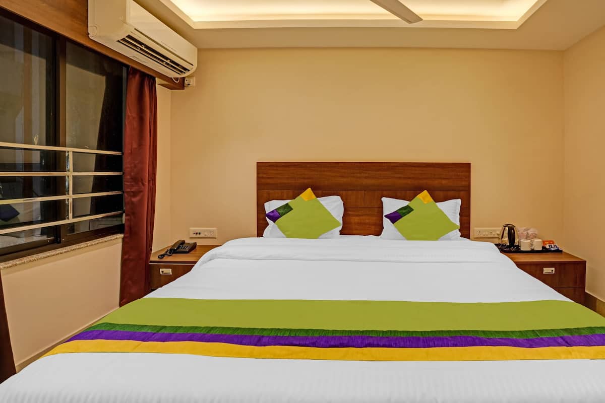 Quarto de hotel com uma cama, mesa de cabeceira, telefone, chaleira e ar condicionado.