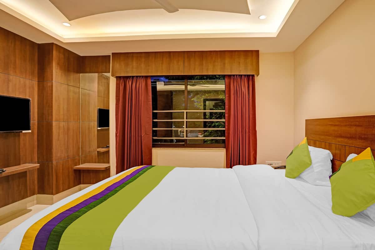 Quarto de hotel moderno com uma cama grande, painéis de parede de madeira, uma TV fixada na parede e uma janela com cortinas vermelhas.