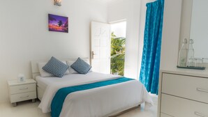 Quarto com cama, mesa de cabeceira, cômoda, janela com vista para vegetação e um quadro na parede.
