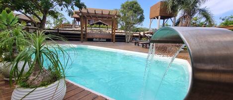 Piscina com um elemento aquático, rodeada por um deck de madeira e plantas em vasos.
