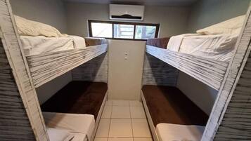 Quarto compacto com duas beliches, uma janela pequena e unidade de ar condicionado central.