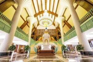 Um hall imponente com escadaria central, colunas grandes e um candelabro.