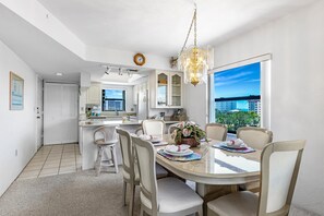 Uma cozinha moderna com armários brancos, uma área de refeições com mesa e cadeiras redondas, e vista para a cidade através de uma grande janela.