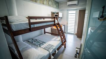 Quarto com beliche, escrivaninha e cadeira, janela com persianas e porta com puxador.