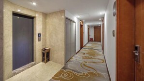 Corredor de hotel com paredes de mármore, carpete estampado e portas de madeira.