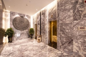 Um corredor com piso de mármore, design circular nas paredes, área de recepção e elevador dourado.