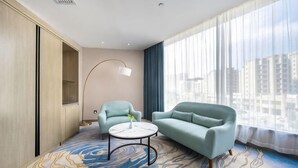 Quarto de hotel moderno com uma janela grande, duas poltronas, uma mesa de centro redonda e piso com padrão marmorizado.