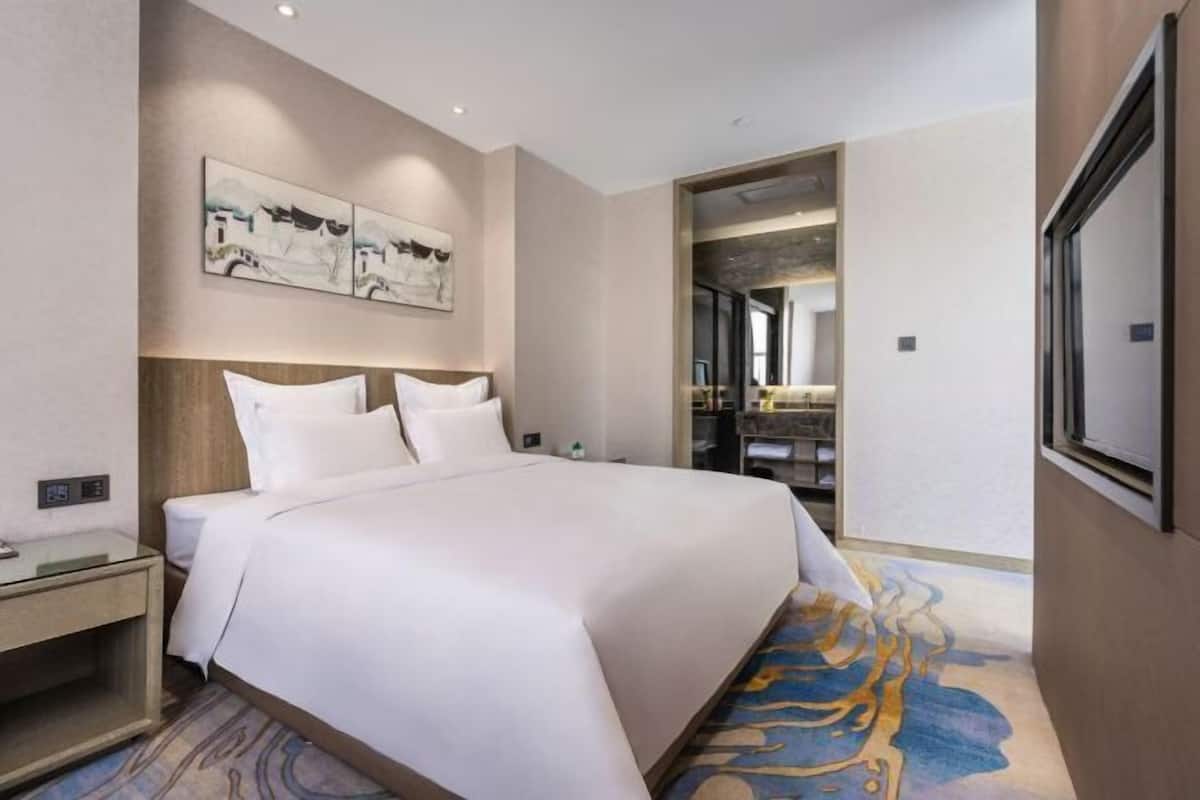 Quarto de hotel com uma cama grande, uma mesinha de cabeceira, um espelho e obras de arte na parede.