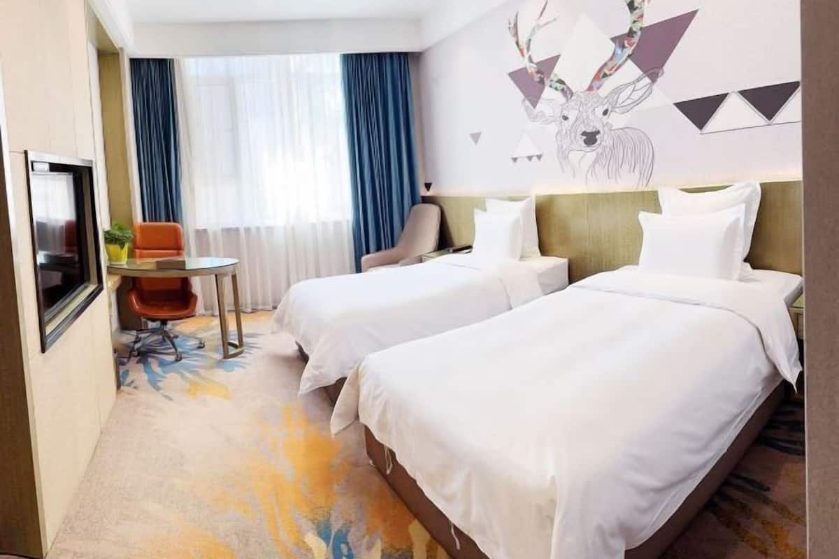 Quarto de hotel com duas camas, uma escrivaninha com cadeira, televisão e um mural decorativo na parede.