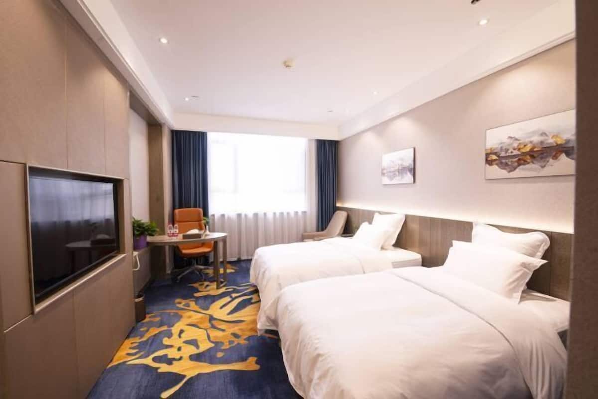 Quarto de hotel com duas camas, uma escrivaninha, uma cadeira, uma televisão e uma janela com cortinas.