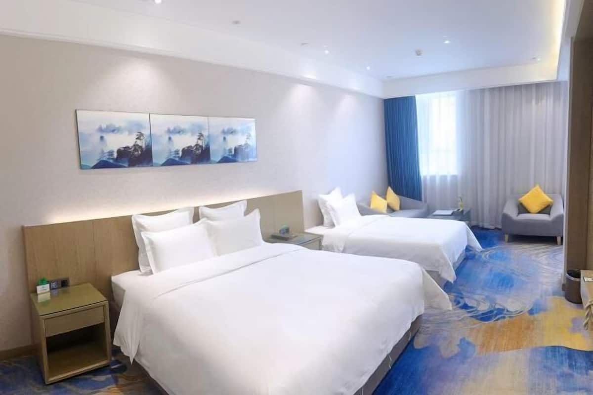 Quarto de hotel com duas camas, uma mesa de cabeceira, uma cadeira e uma obra de arte na parede.