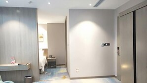 Quarto de hotel com cama, escrivaninha, lixeira e guarda-roupa.