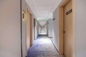 Corredor de hotel com portas em ambos os lados, piso coberto por carpete e teto de cor clara.