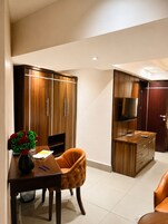 Quarto moderno com guarda-roupa de madeira, televisão na parede, mesa de jantar com um vaso de flores e uma poltrona de couro.
