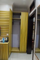 Quarto com guarda-roupa de madeira, uma pequena mesa com chaleira e garrafa, e um espelho na parede.