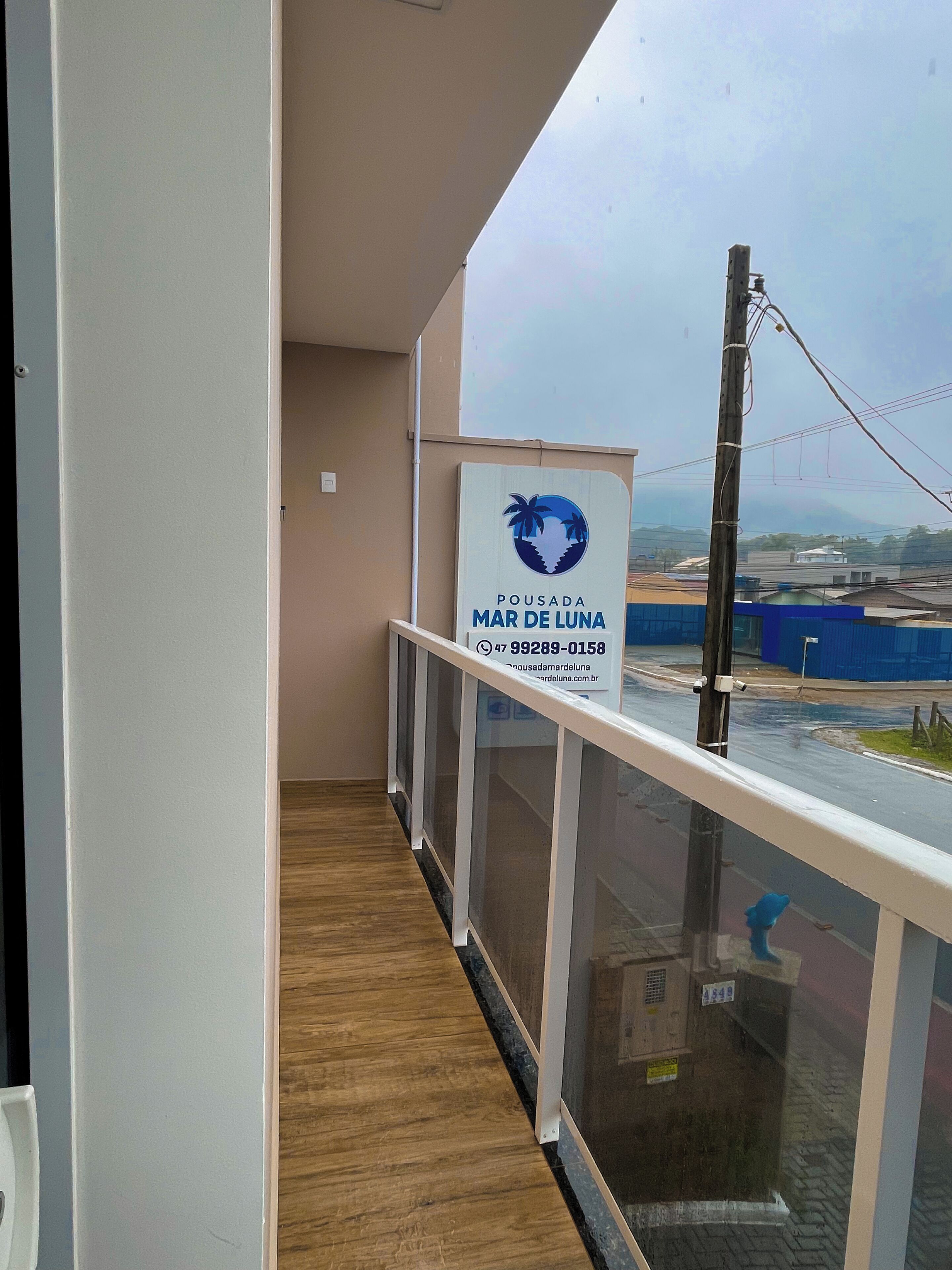 Uma varanda com uma placa indicando 'Pousada Mar de Luna' e vista para a rua e edifícios.