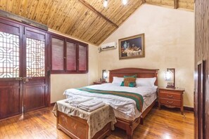 Quarto com teto de madeira, cama com cabeceira de madeira, mesa de cabeceira, ar condicionado fixado na parede e janela com persianas de madeira.