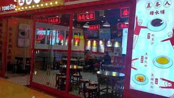Restaurante com fachada vermelha e janelas de vidro, exibindo um cardápio e oferecendo mesas ao ar livre.